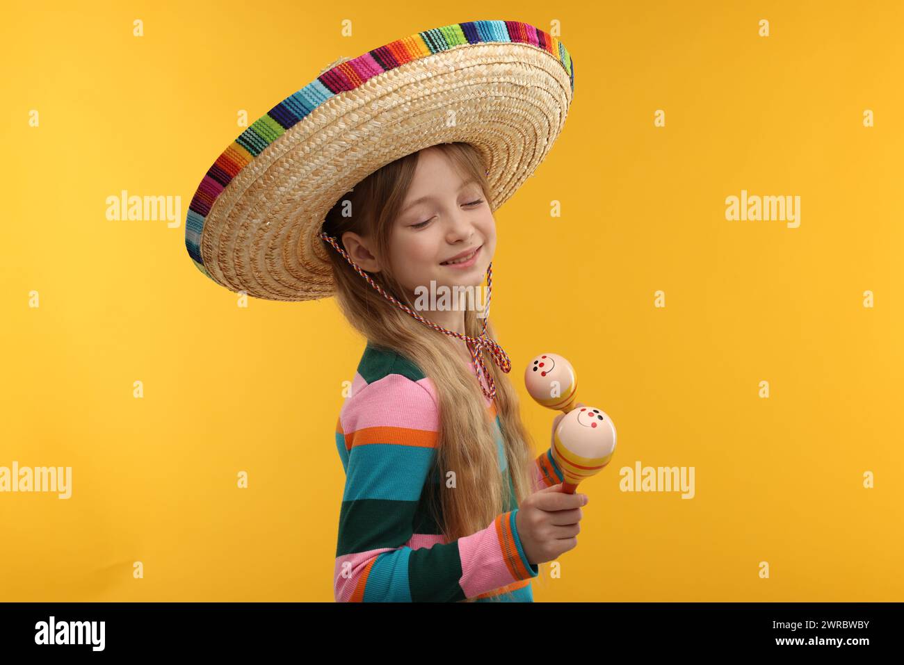 Cute girl in Mexican sombrero hat dancing with maracas on orange ...