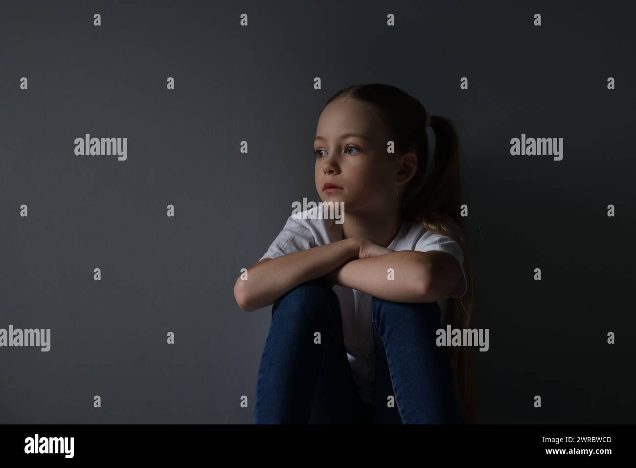 Sad girl sitting near dark grey background, space for text Stock Photo ...