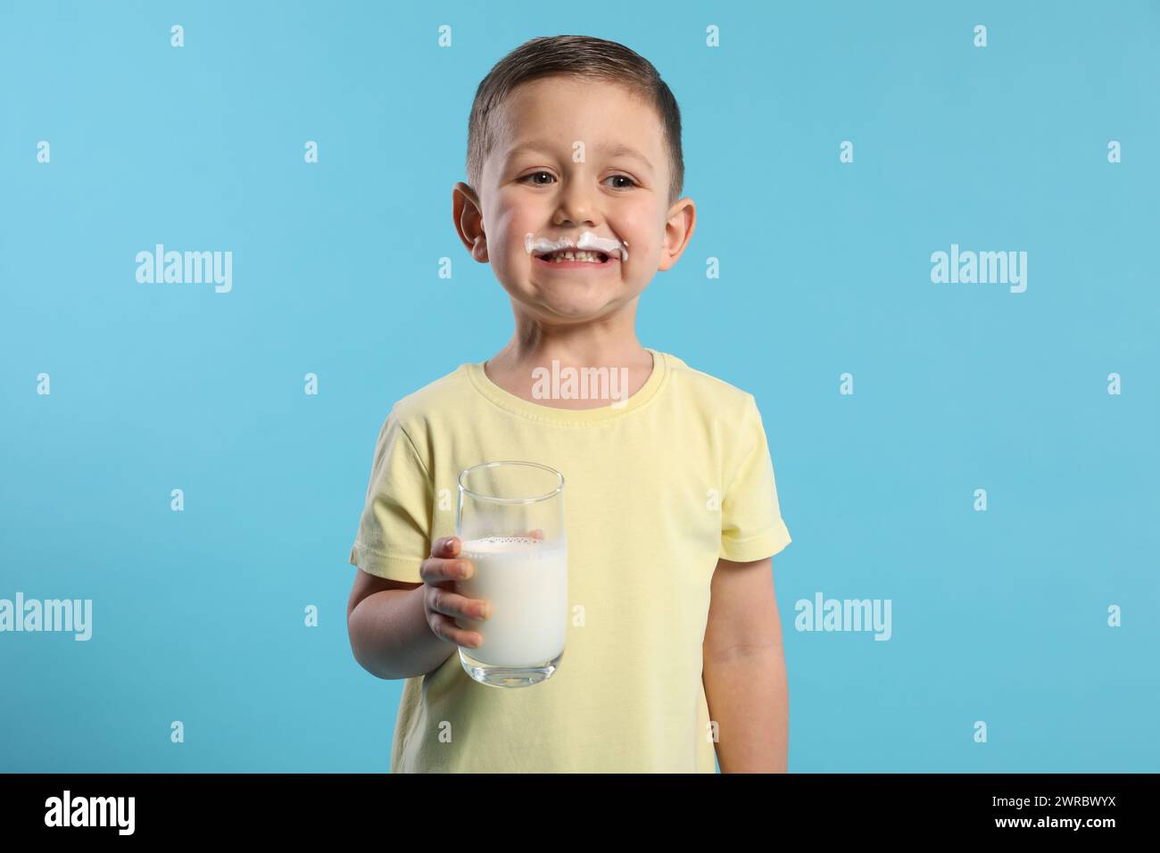 Cute boy with milk mustache holding glass of tasty dairy drink on light ...