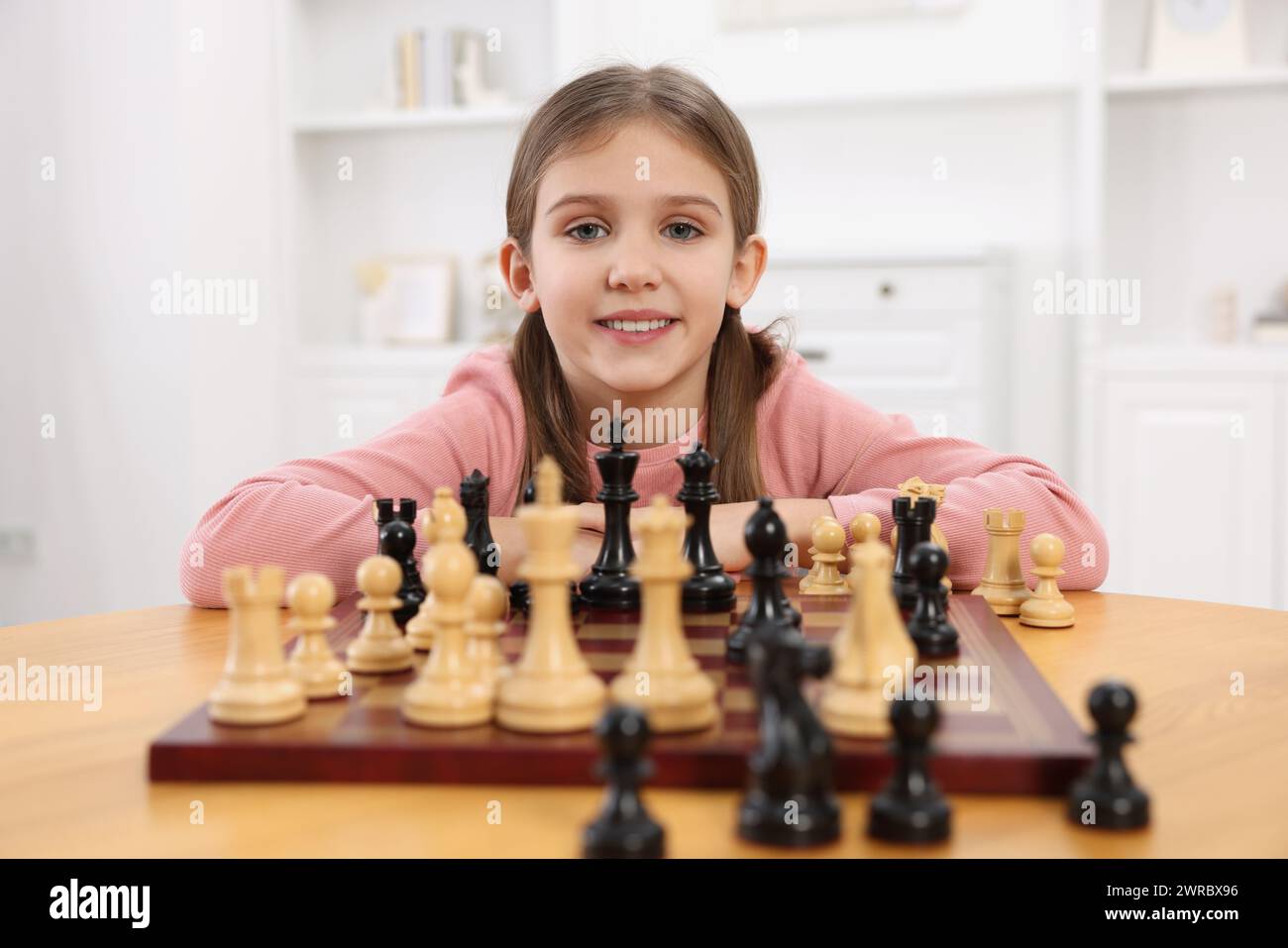 Cute girl playing chess at table in room Stock Photo - Alamy