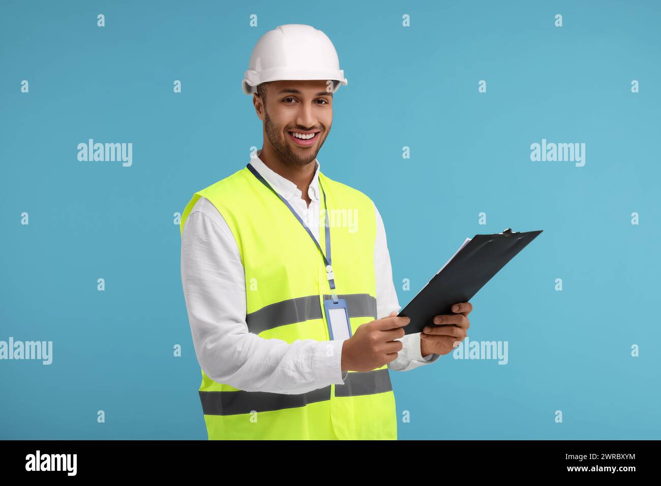 Engineer in hard hat holding clipboard on light blue background Stock ...