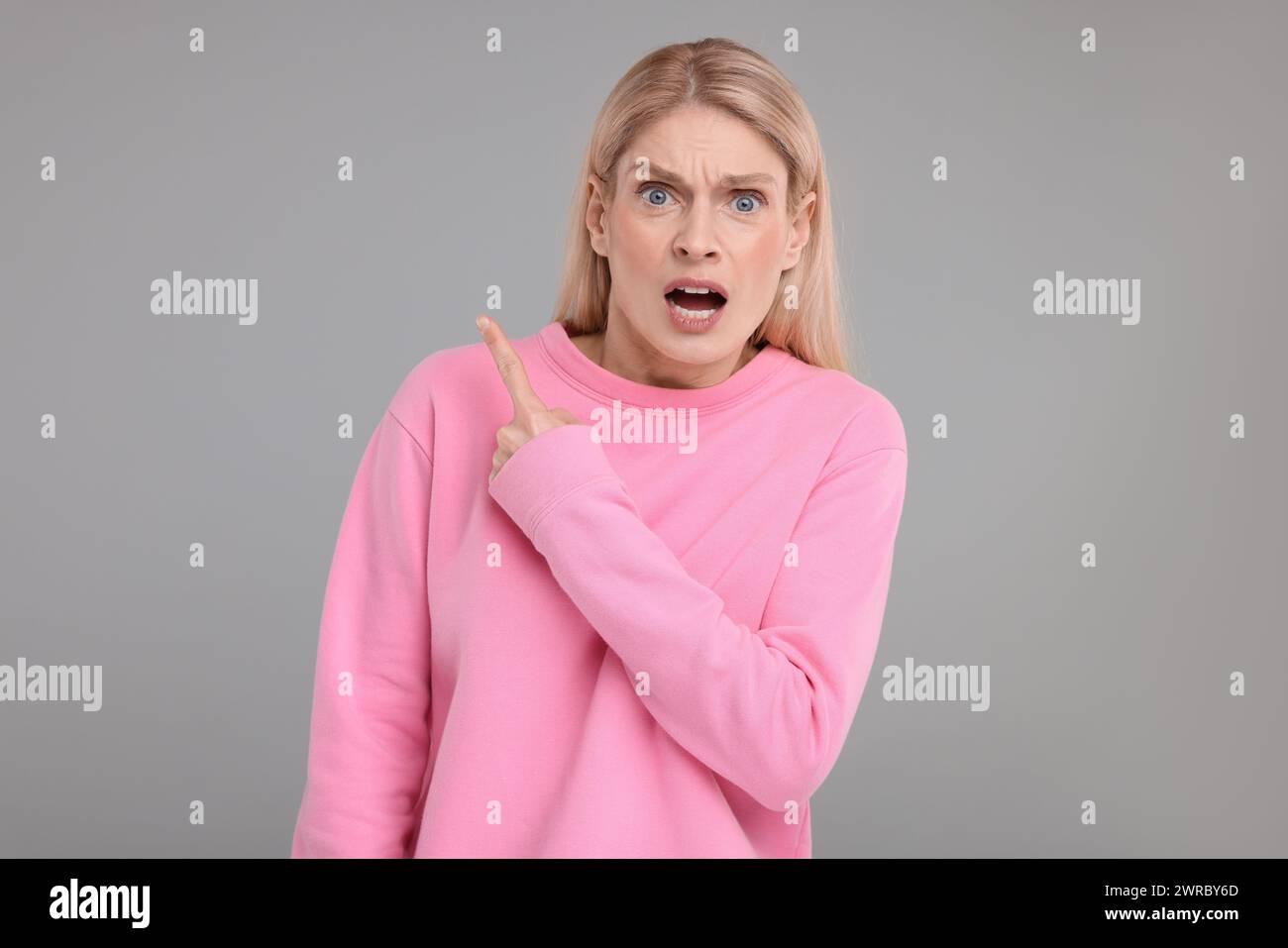 Surprised woman pointing at something on grey background Stock Photo ...