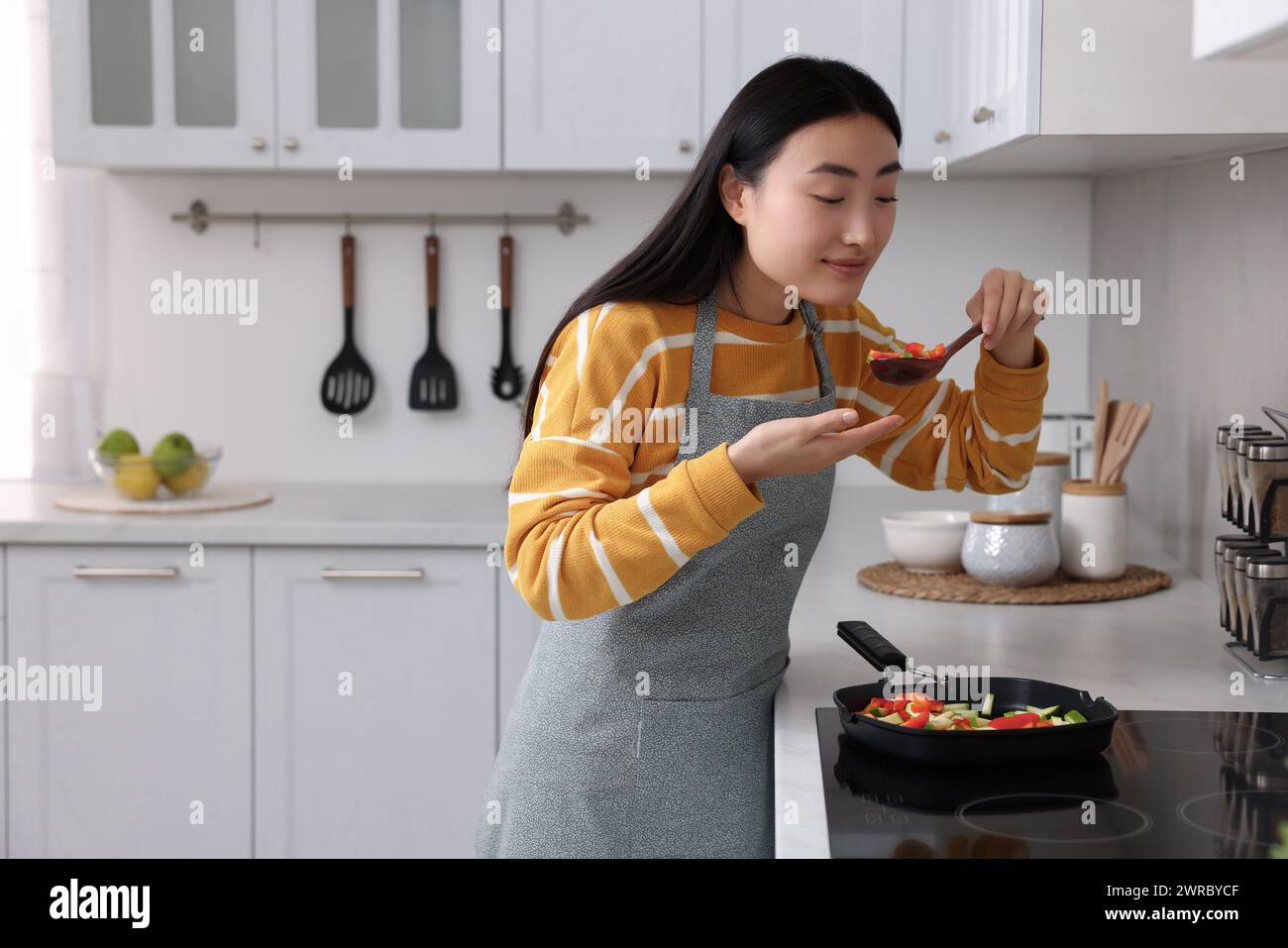 Beautiful woman cooking and tasting vegetable dish in kitchen. Space for text Stock Photo - Alamy