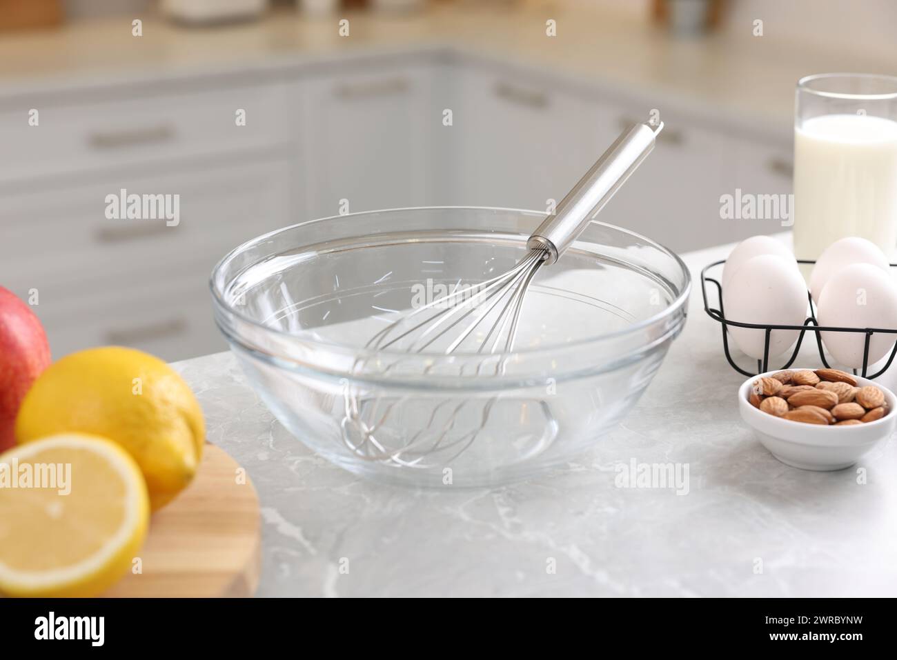 Metal whisk, bowl and different products on gray marble table in ...