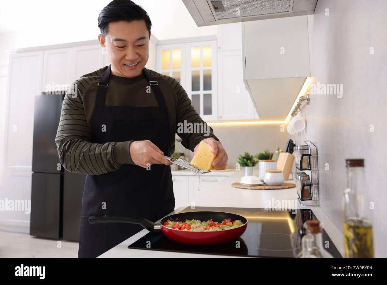 Cooking process. Man grating cheese into frying pan in kitchen Stock ...