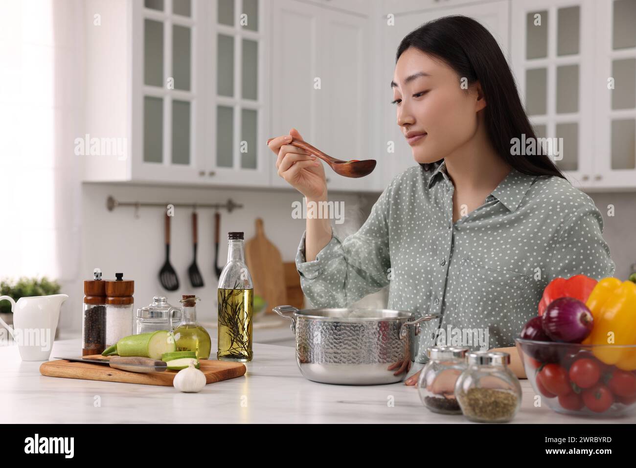Beautiful woman tasting food after cooking in kitchen Stock Photo - Alamy