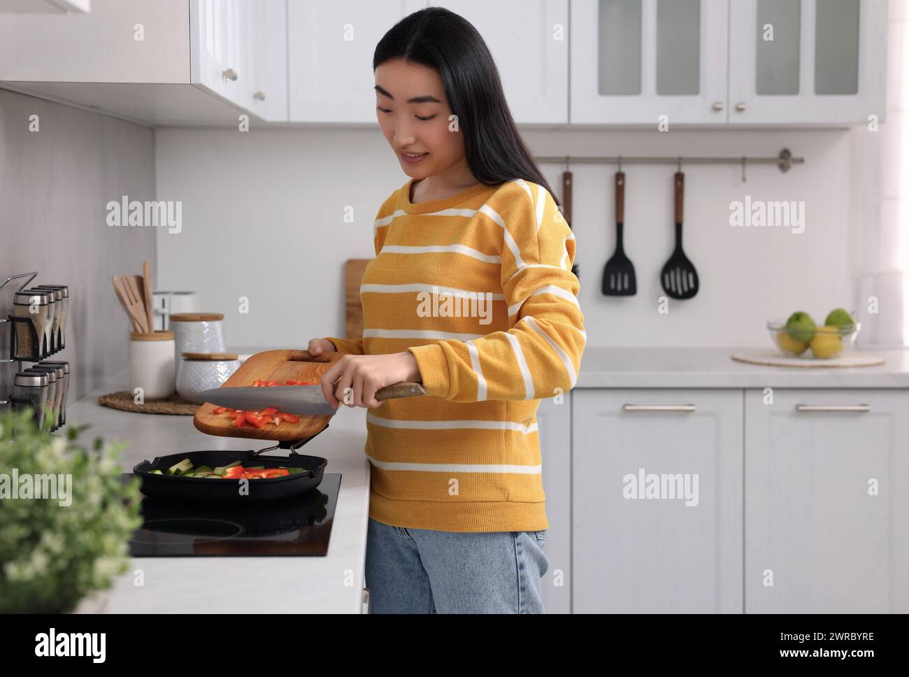 Cooking process. Smiling woman adding cut bell pepper into pan with ...