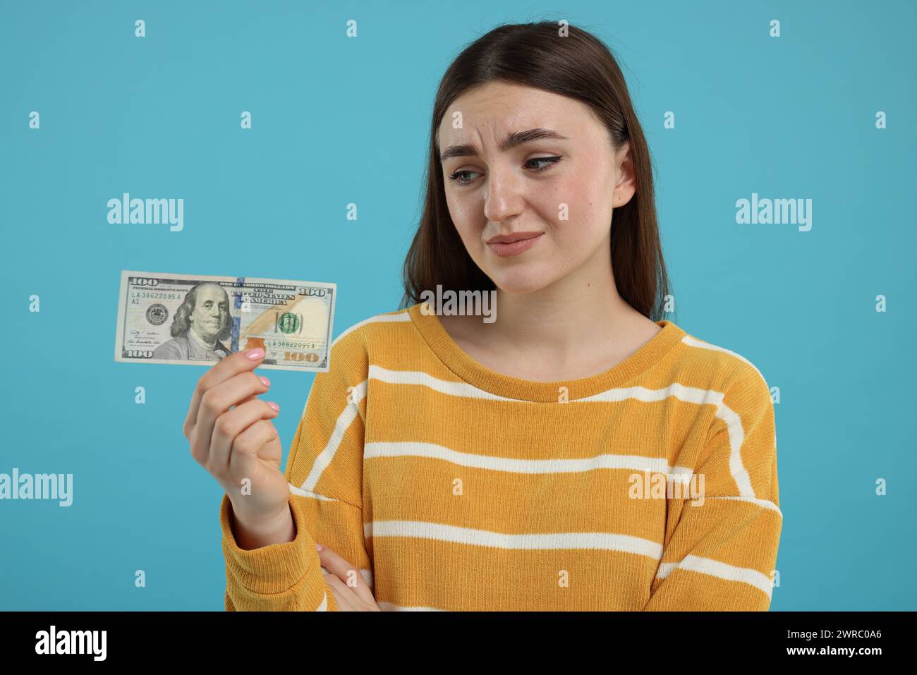 Sad woman with dollar banknote on light blue background Stock Photo - Alamy