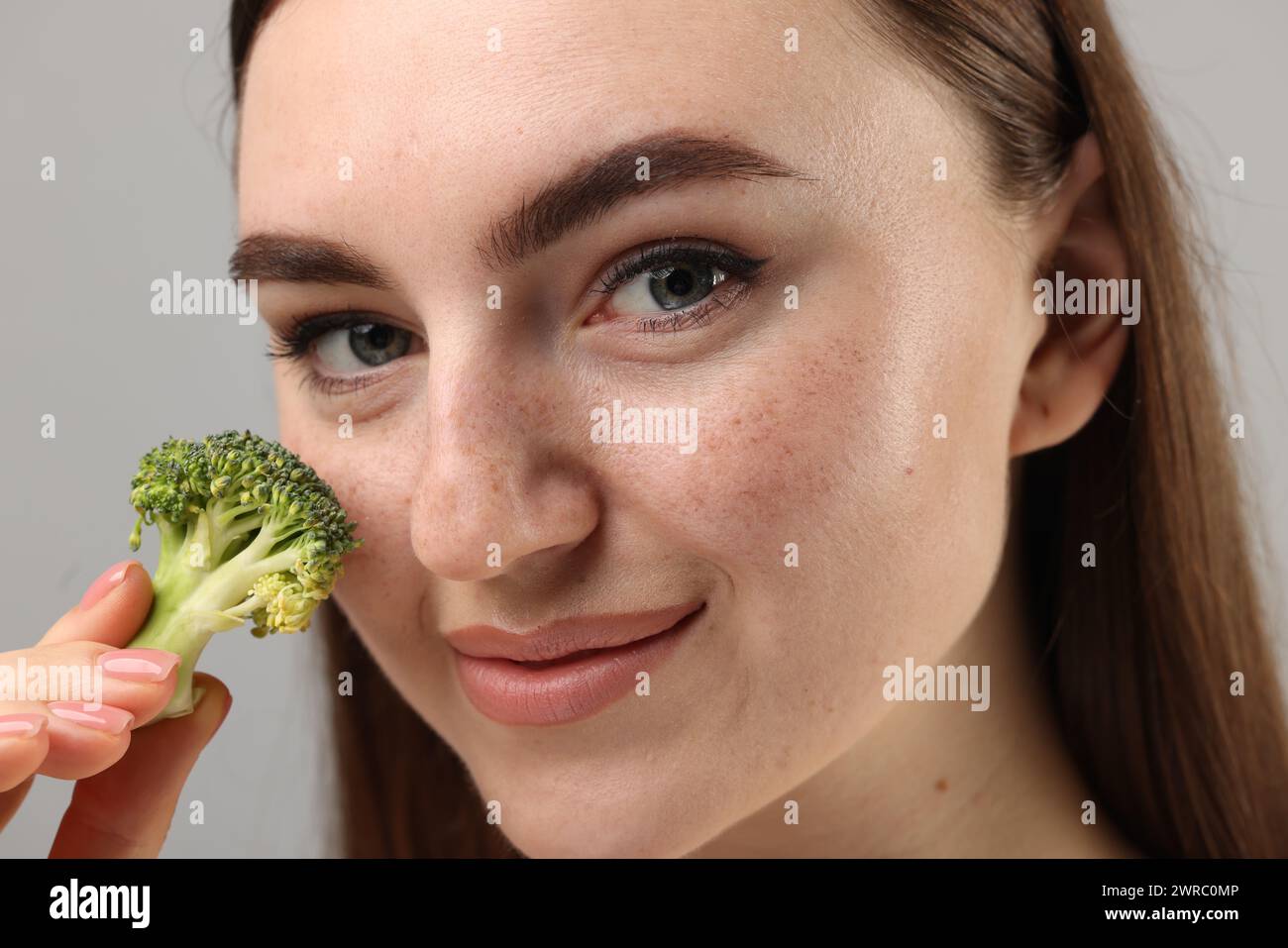 Beautiful woman making fake freckles with broccoli and cosmetic product ...