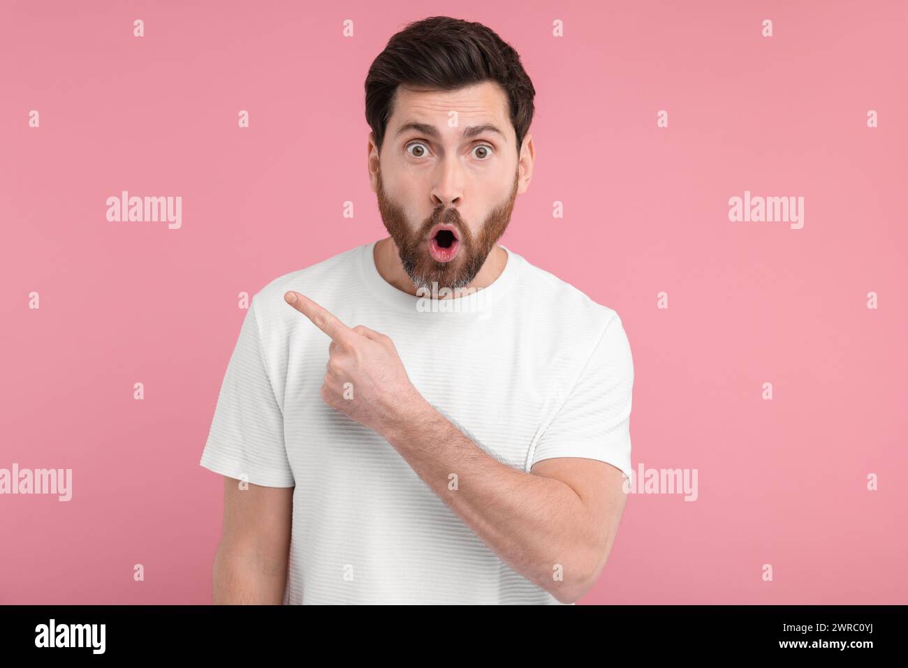 Surprised man pointing at something on pink background Stock Photo - Alamy