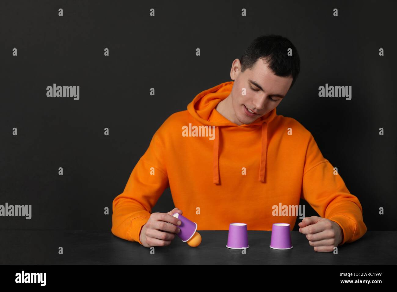 Shell game. Man showing ball under cup at black table Stock Photo - Alamy