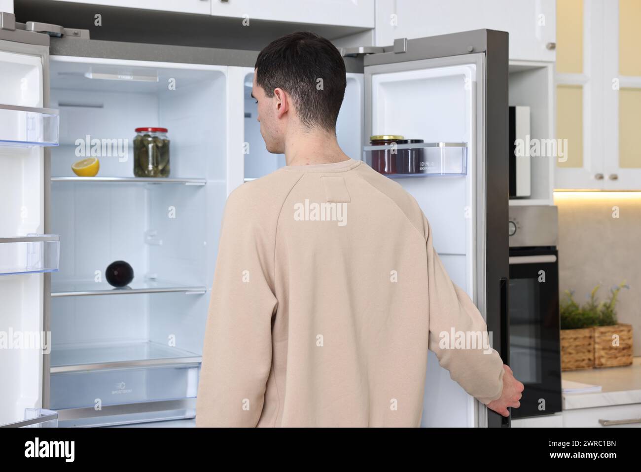 Man near empty refrigerator in kitchen at home, back view Stock Photo ...