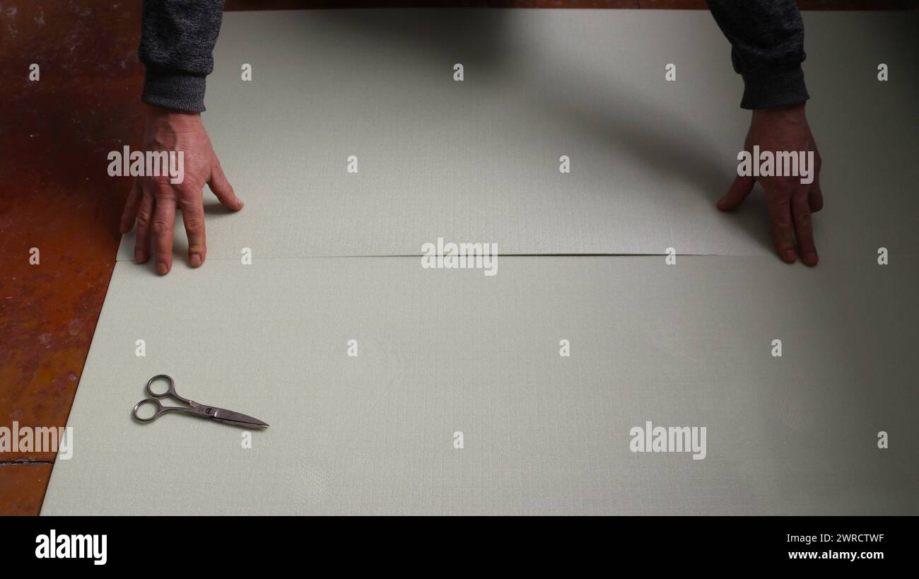 a man connects two greenish polyester sheets on the floor, making an ...