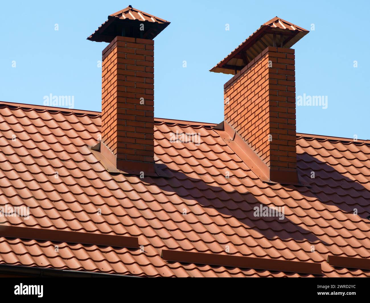 A brick chimneys on a brown metal tile roof Stock Photo - Alamy