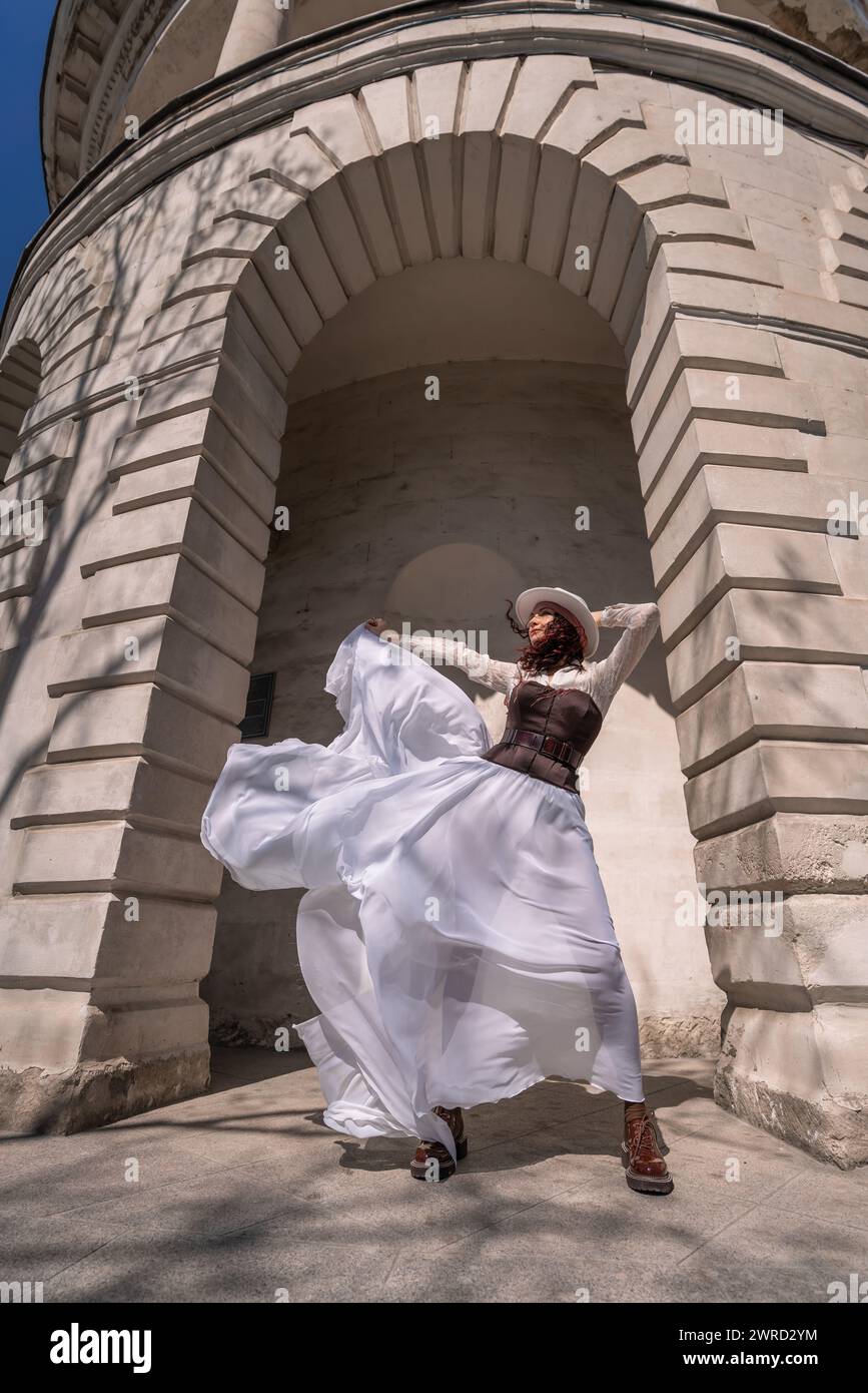 Stylish woman building city. A dancer in a long white skirt dances in ...