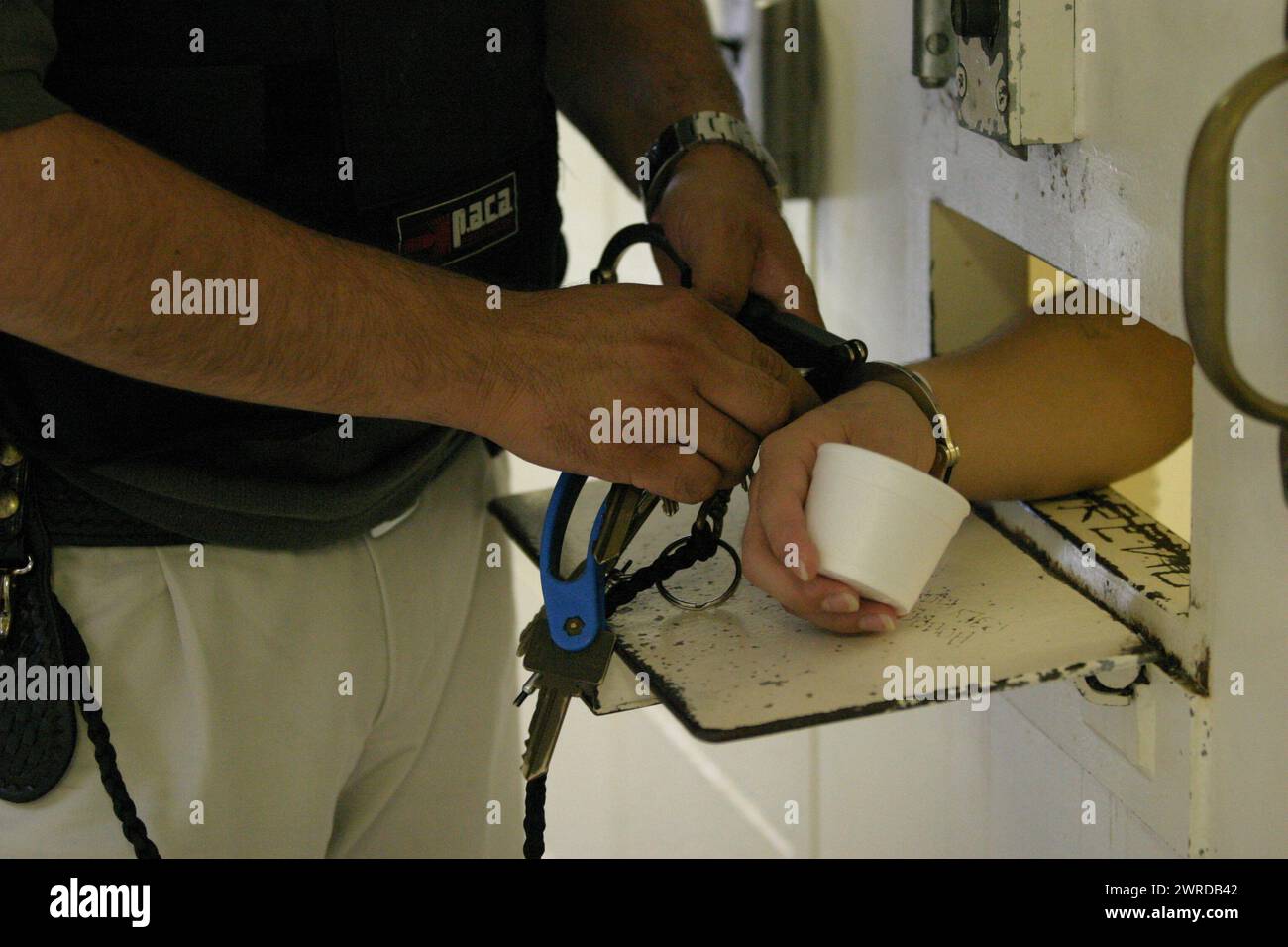A police officer holding a prisoner's hand through a jail cell window ...
