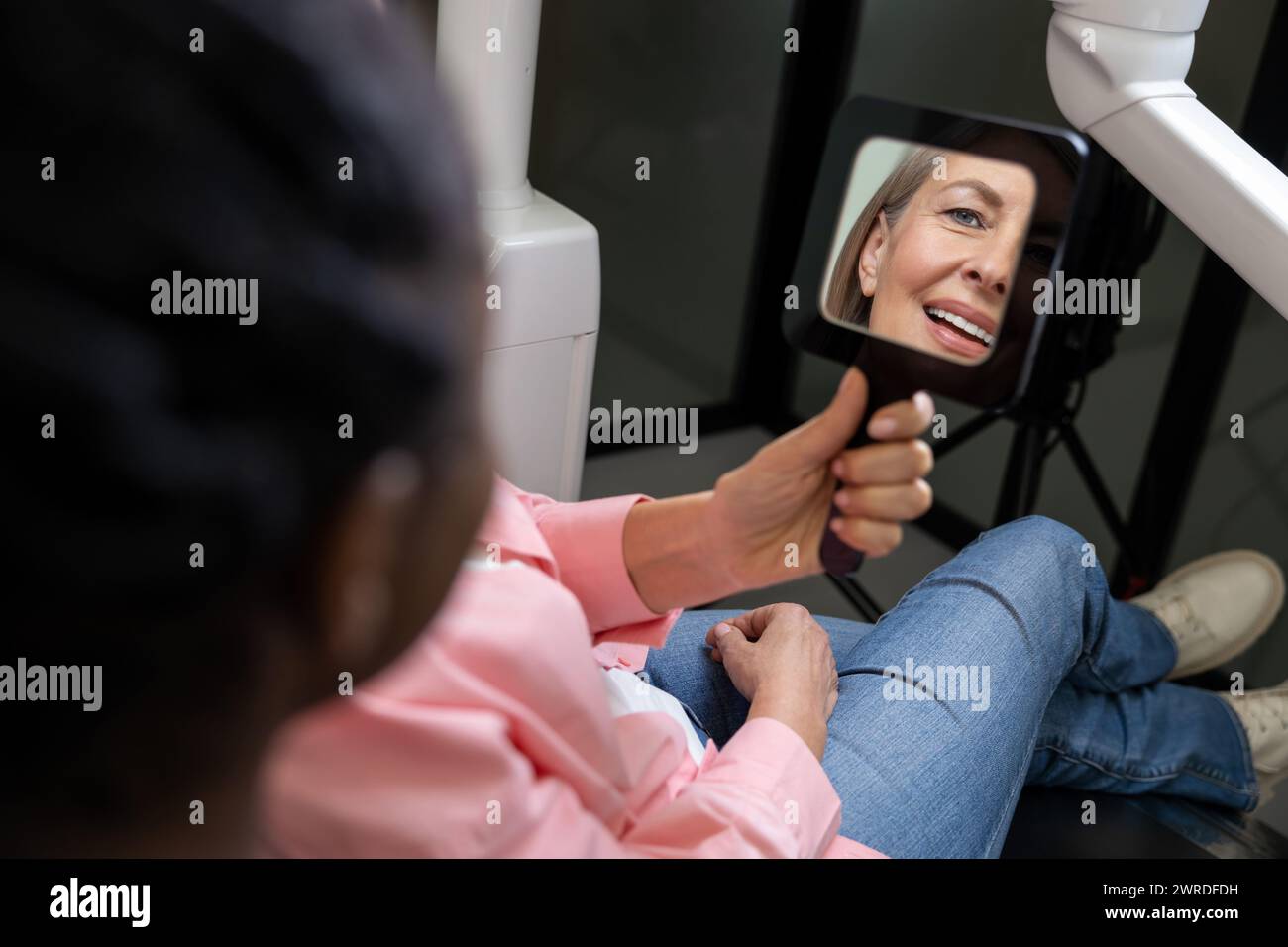 Happy mature female patient looking at mirror after dental treatment in ...