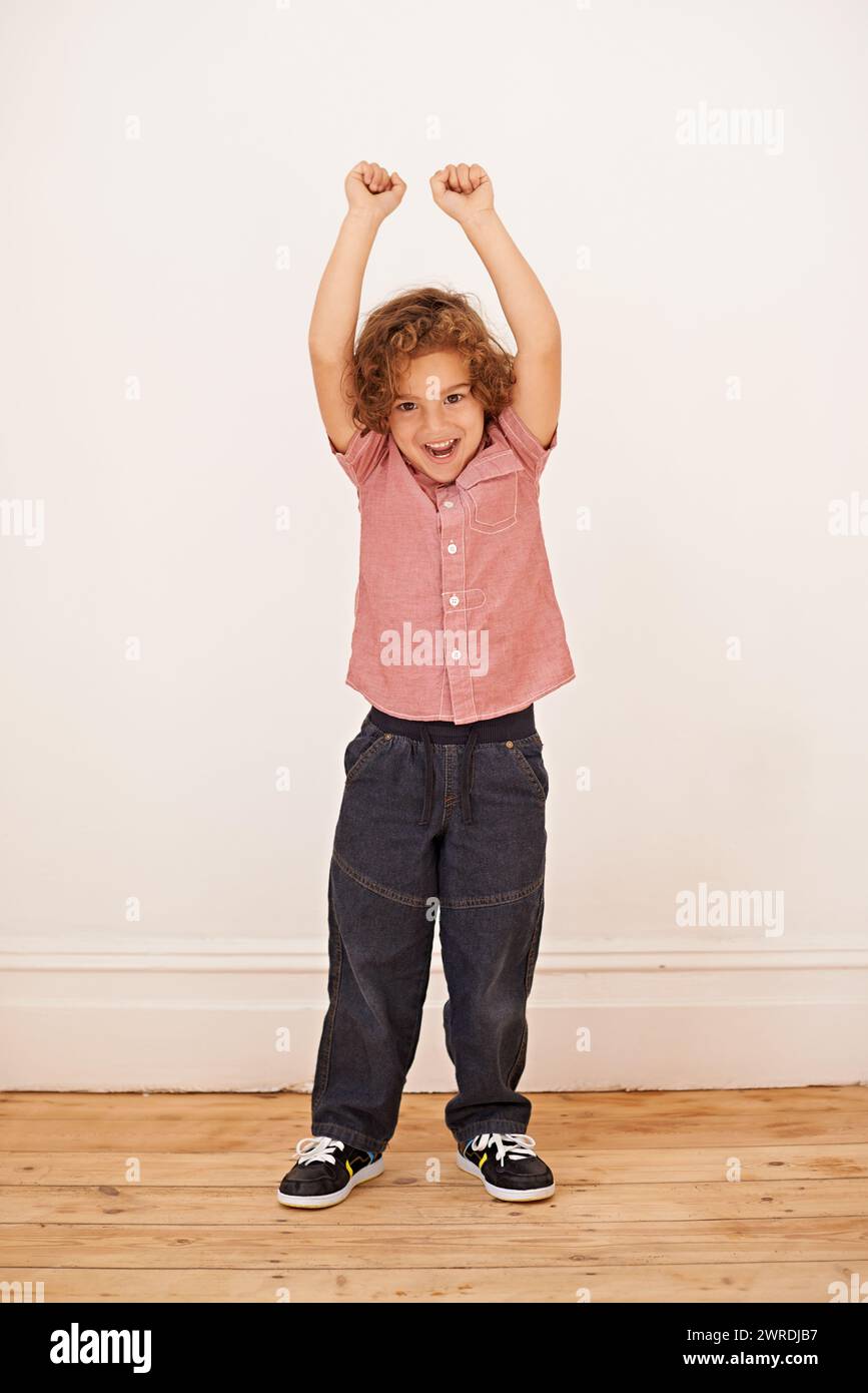 Excited boy, child and portrait with fist in air by wall in family home ...