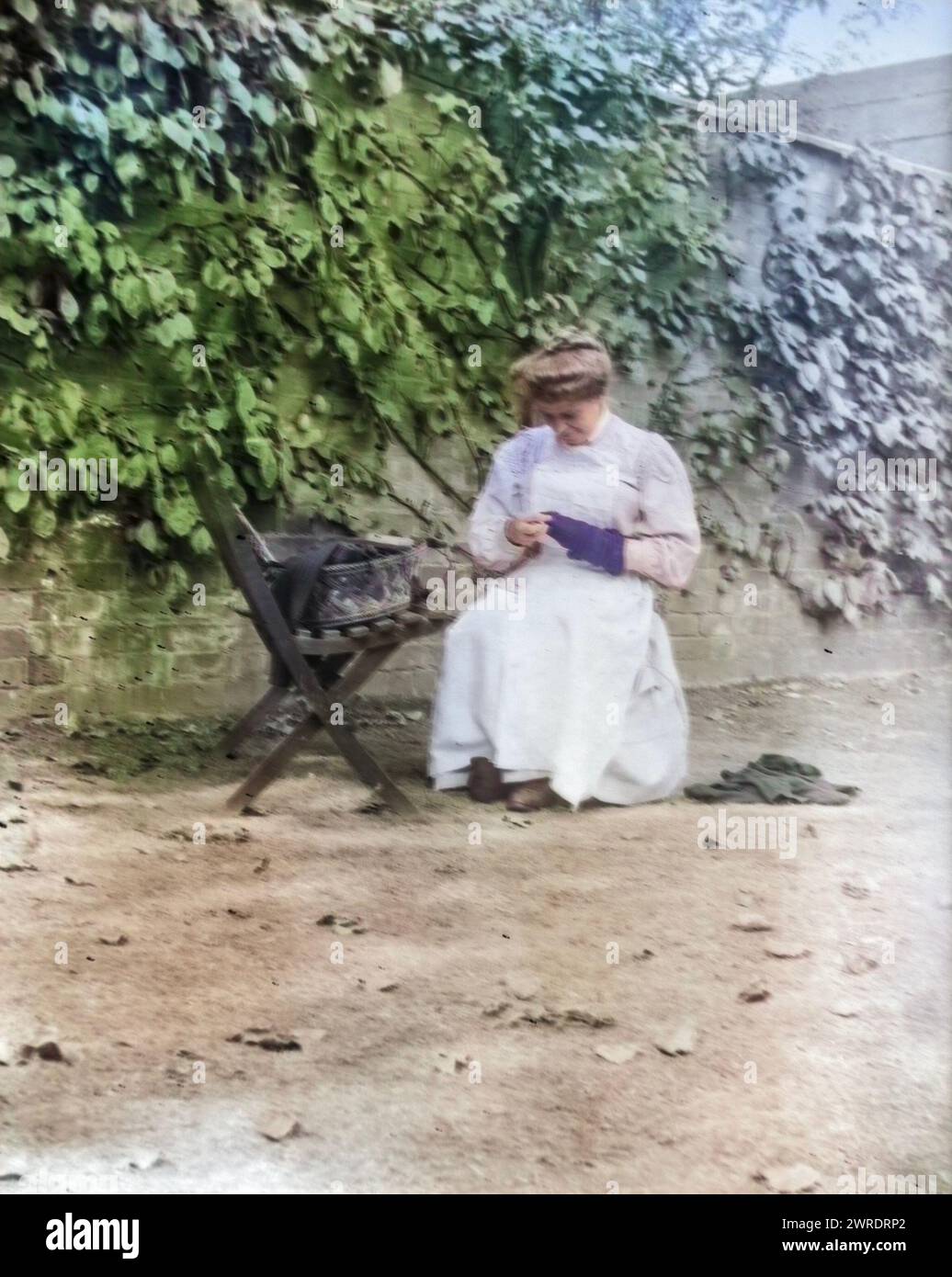 Woman in domestic servant housemaid uniform sitting darning in garden ...
