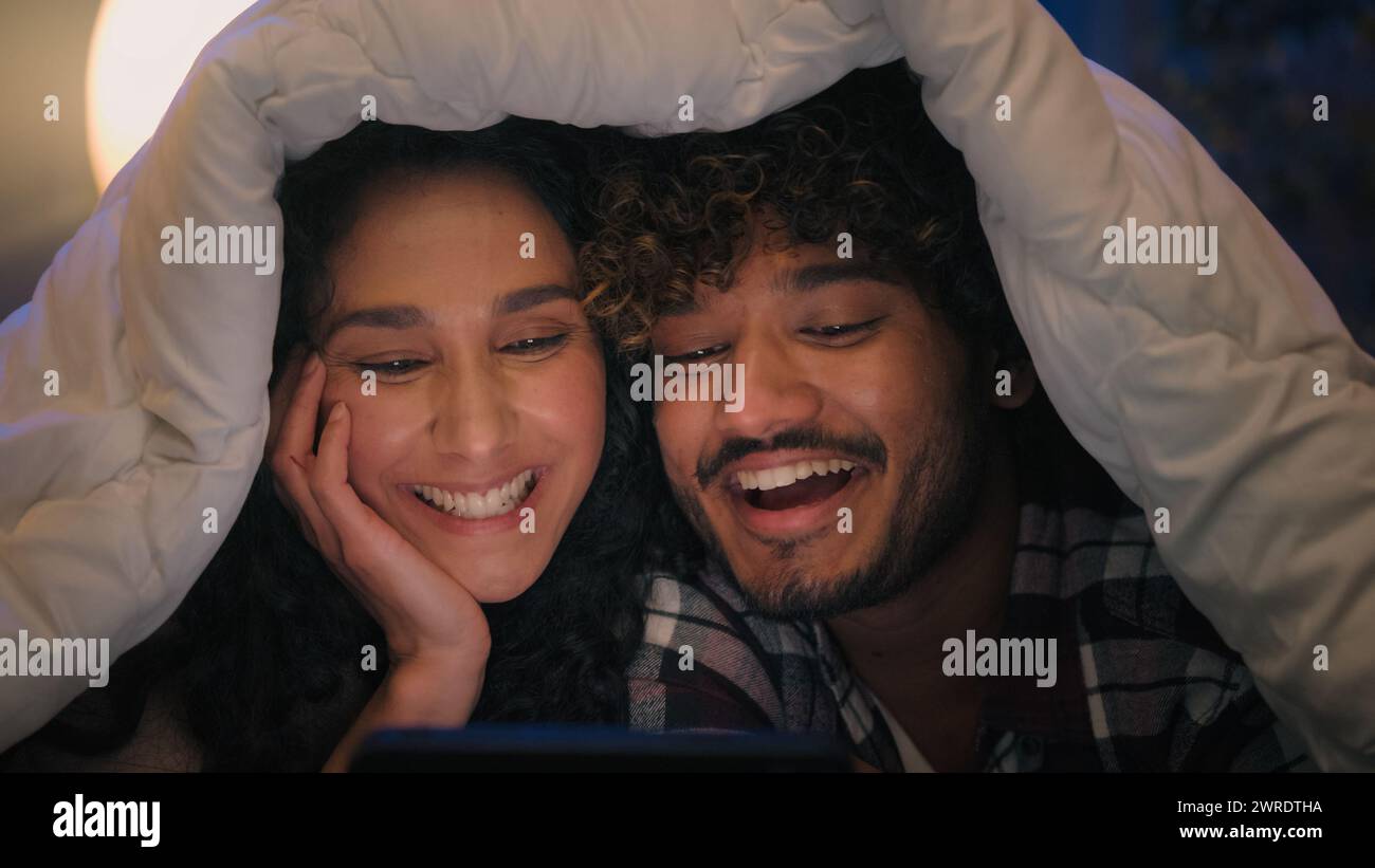 Multiracial happy carefree couple Indian man Hispanic woman watching film movie funny video ...