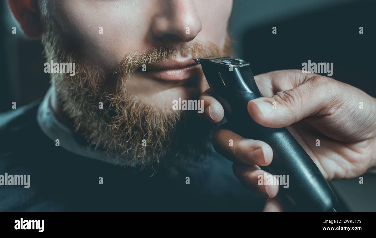 A male hairdresser does a haircut of a beard and a mustache in a ...