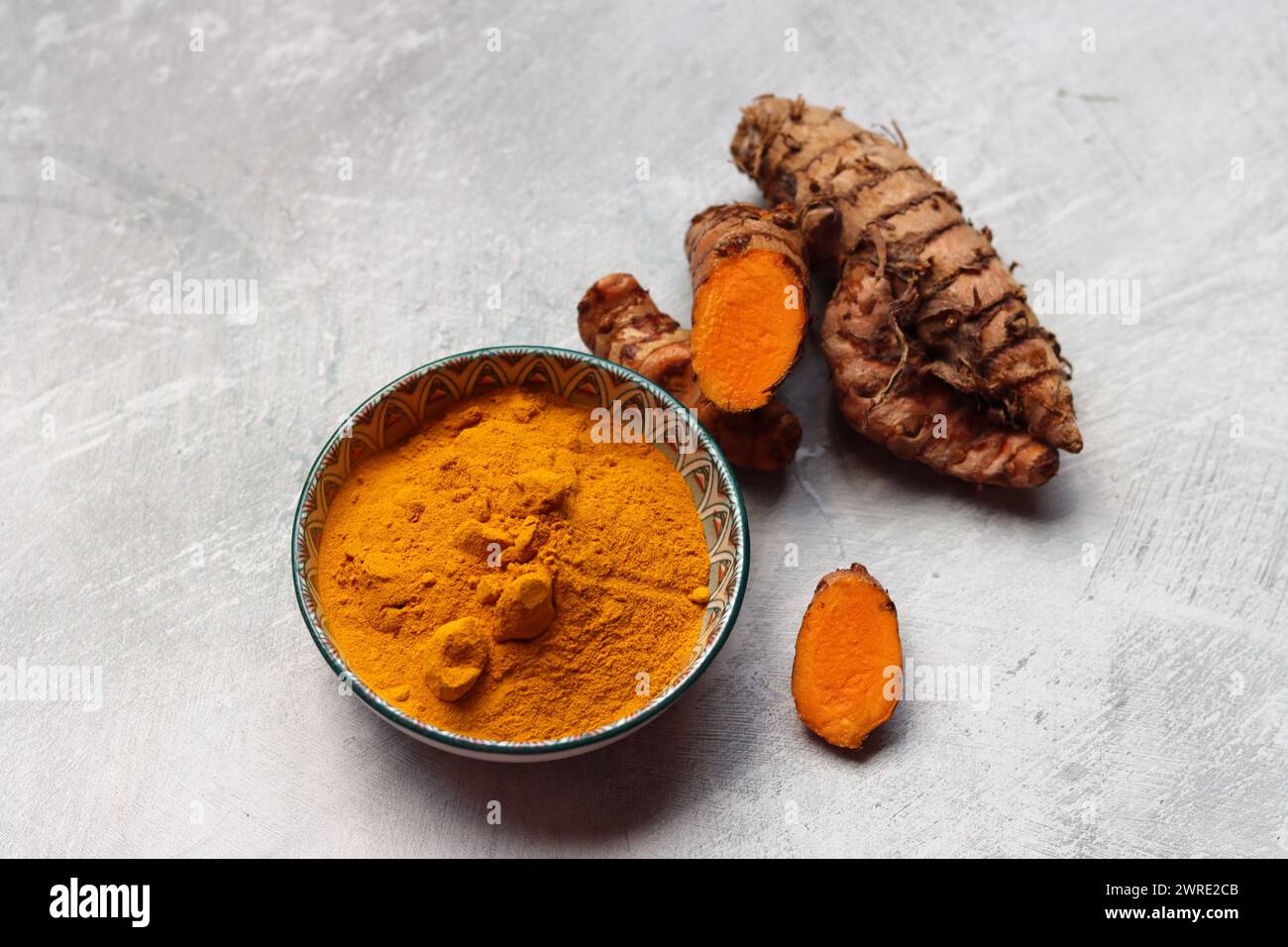 Turmeric powder in bowl and fresh turmeric root on textured background ...