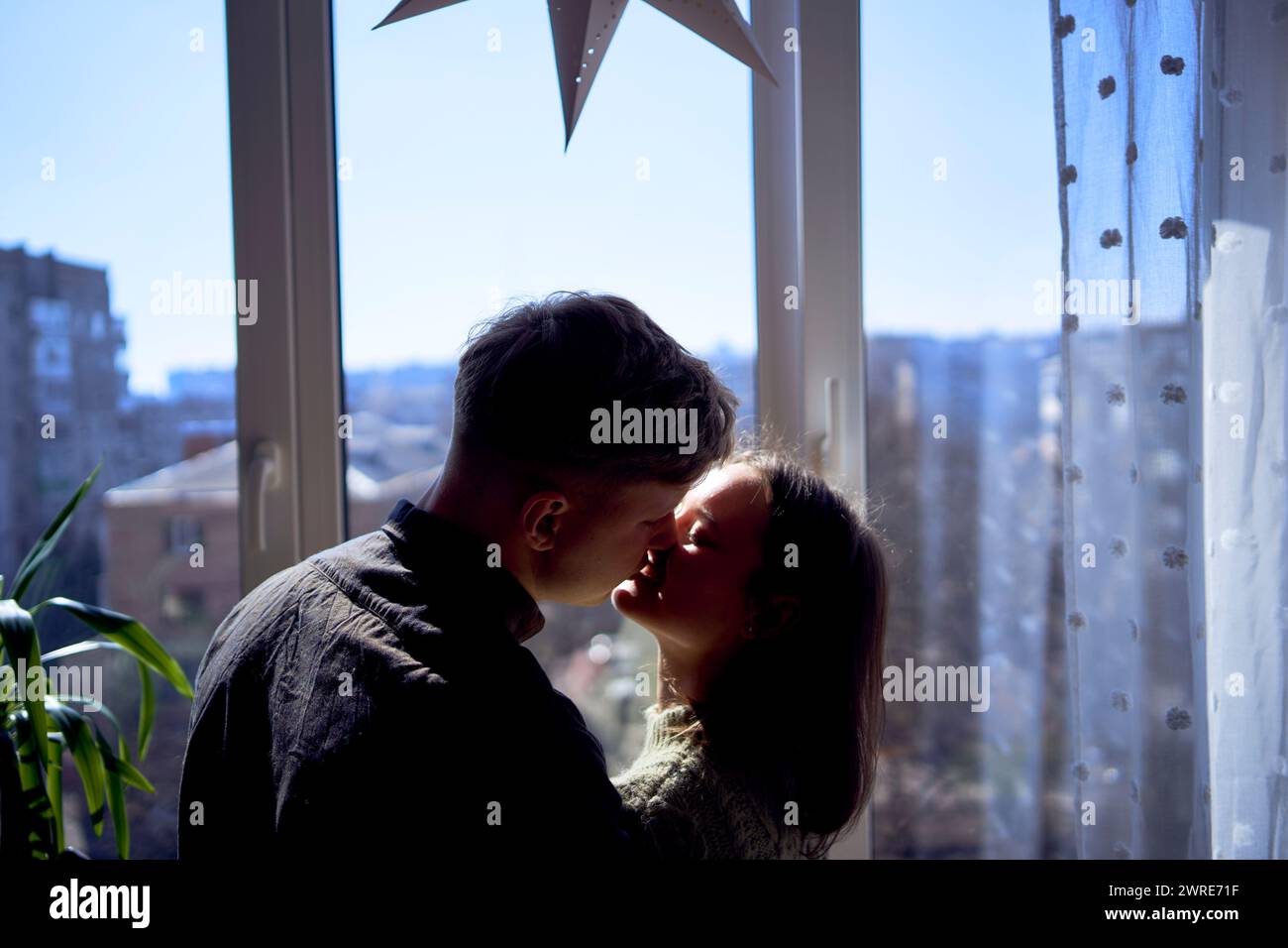 a beautiful young couple kissing in the backlight against the window ...