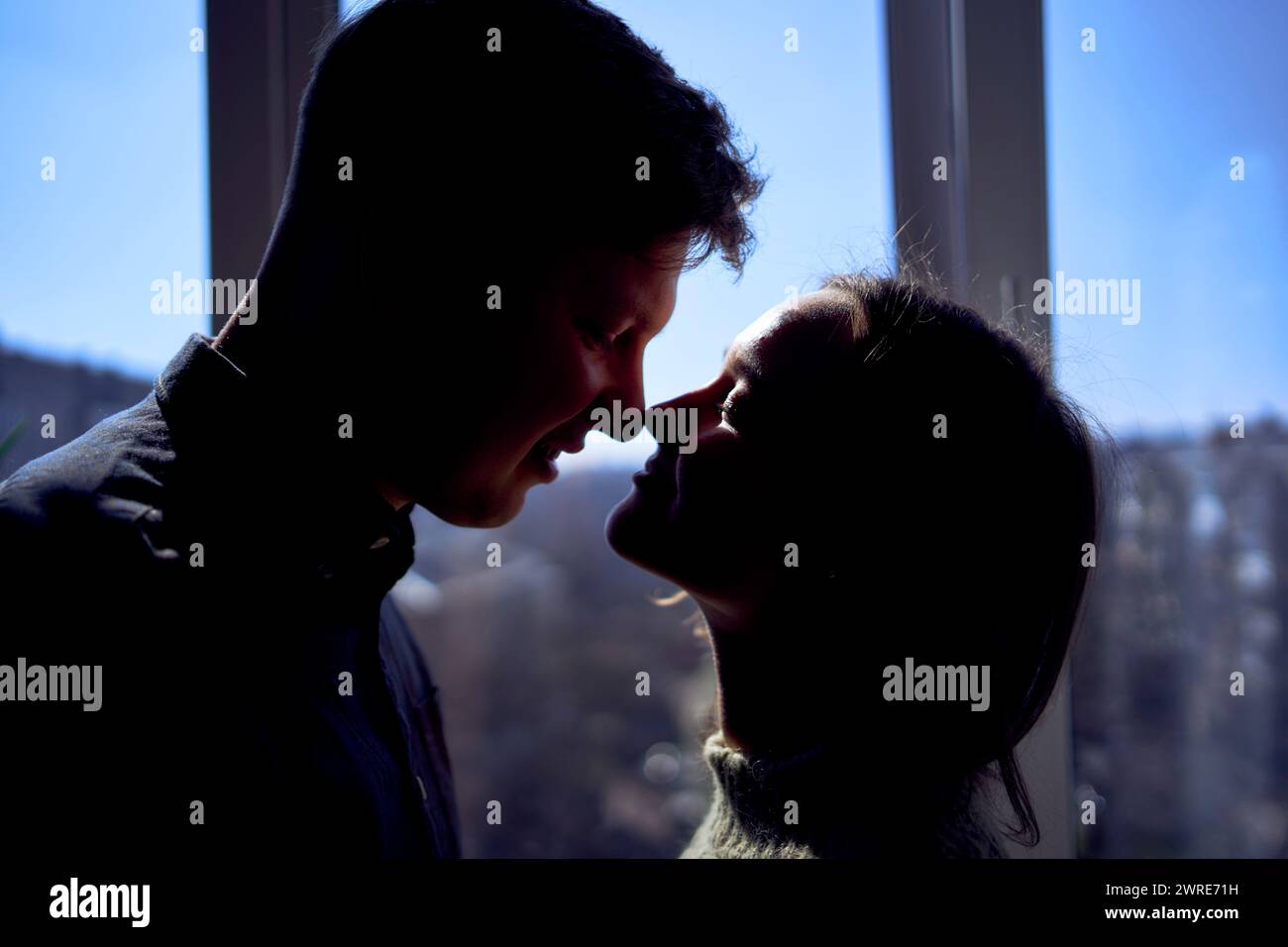 a beautiful young couple kissing in the backlight against the window ...