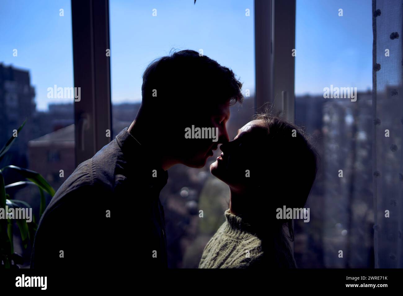 a beautiful young couple kissing in the backlight against the window ...