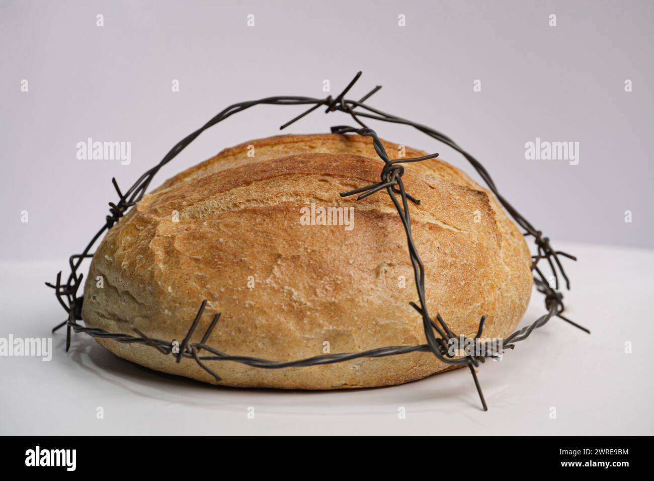 A loaf of round wheat bread wrapped with barbed wire, white background ...