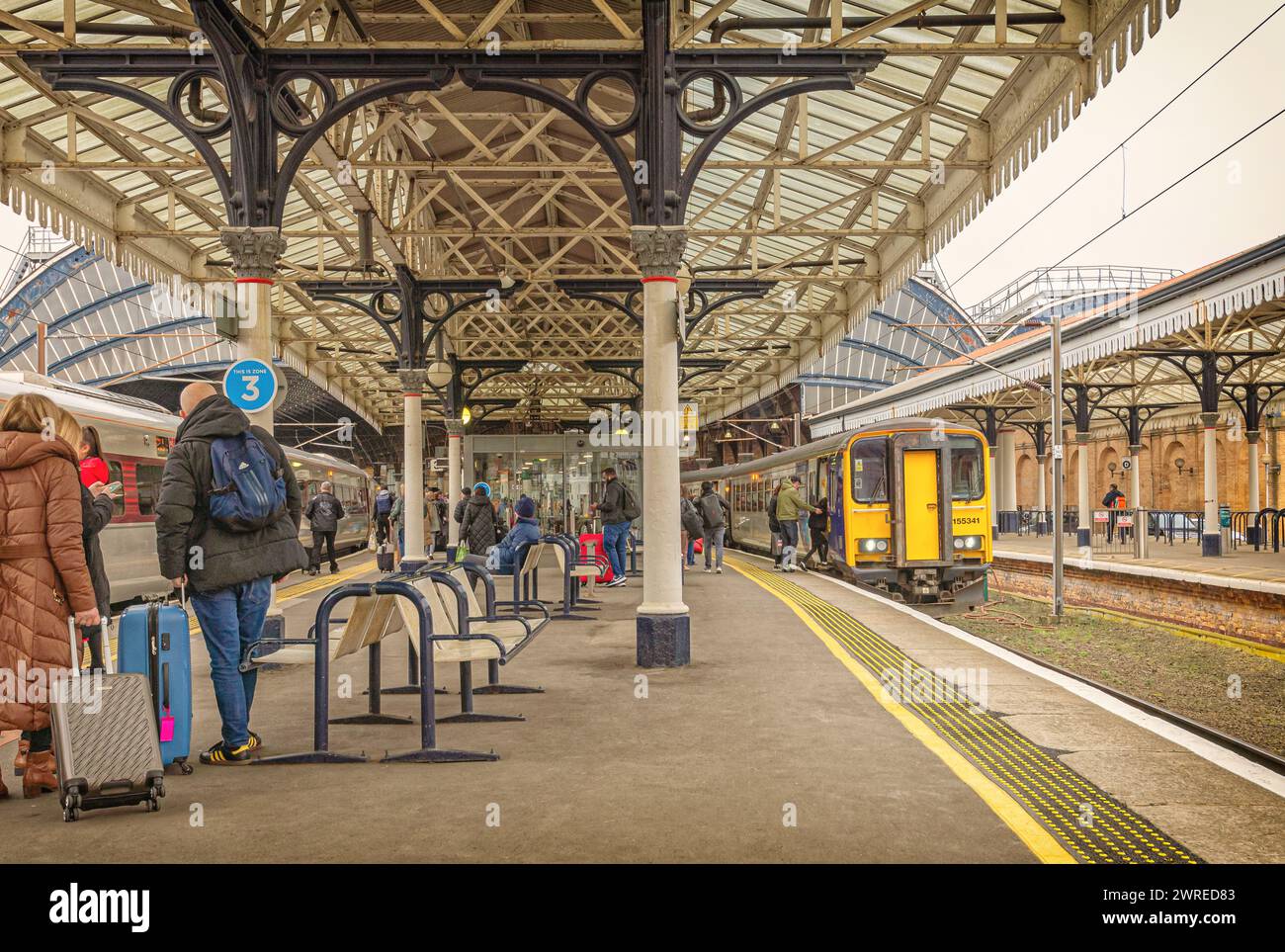 A train waits at a railway station platform beside a historic 19th ...