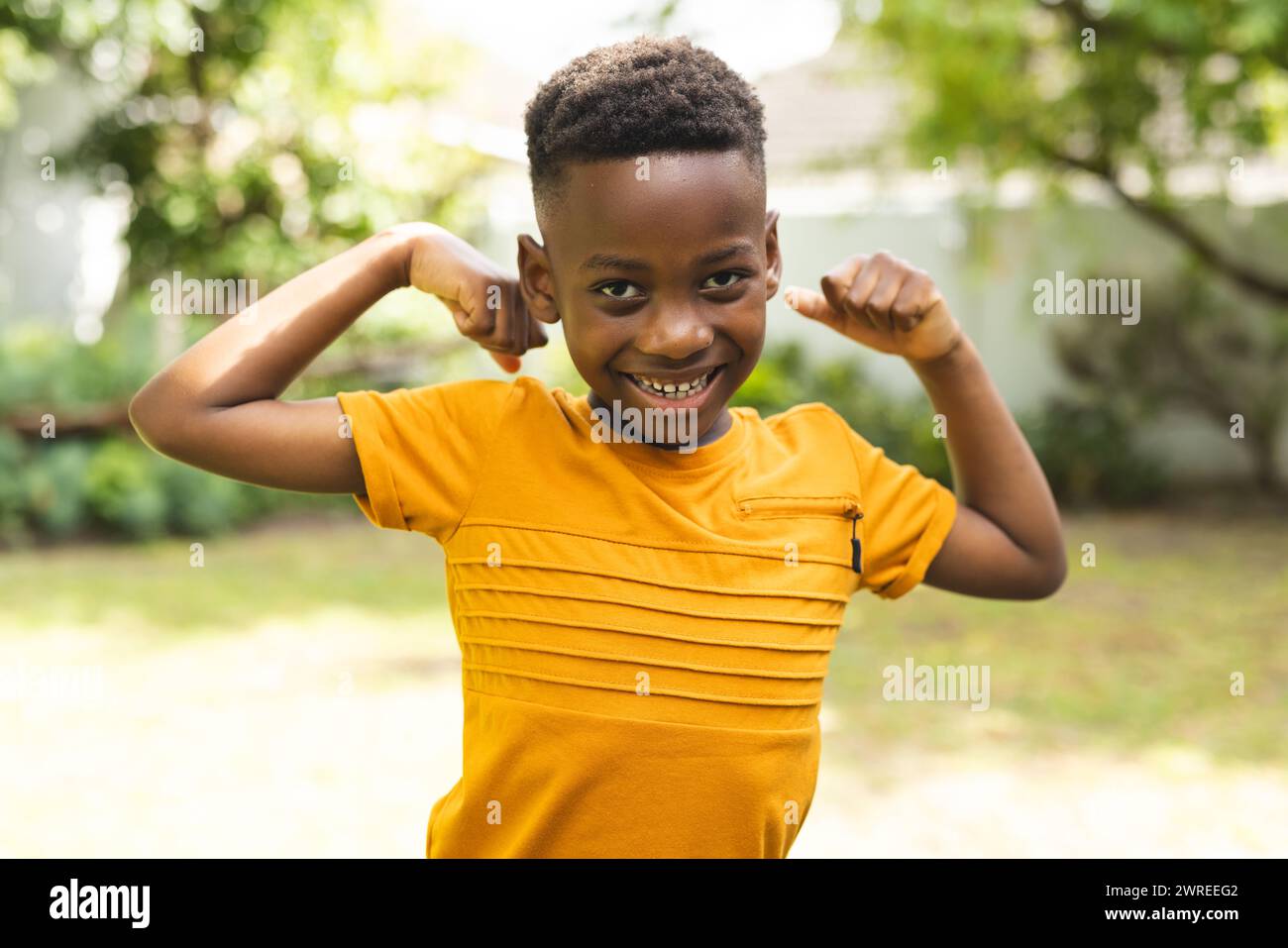 African American boy flexes his muscles with a bright smile in a garden ...