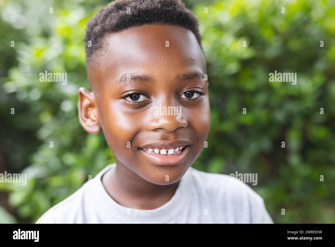 African American boy smiles brightly, surrounded by lush greenery in a ...