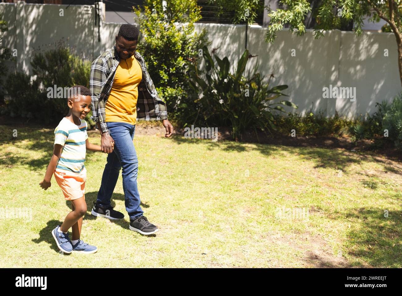 African American father walks with his son, both smiling in a sunny ...