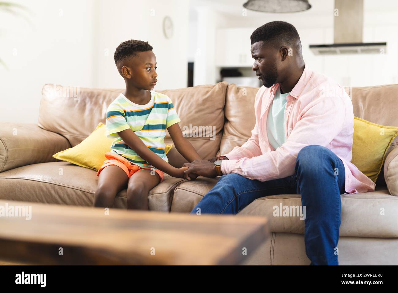 African American Father And Son Sit On A Sofa Holding Hands And