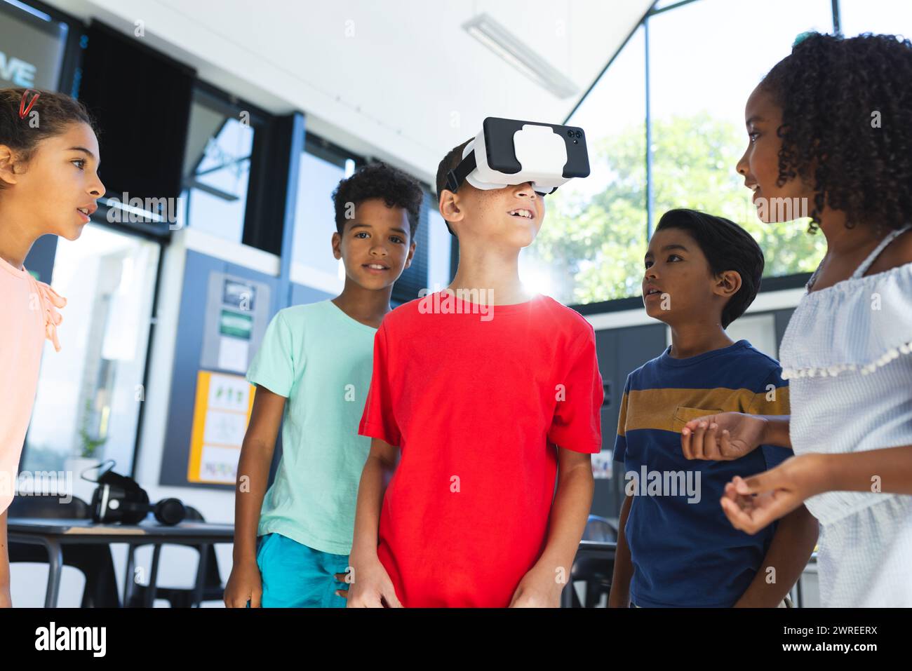 Biracial children are gathered around a boy using a virtual reality ...
