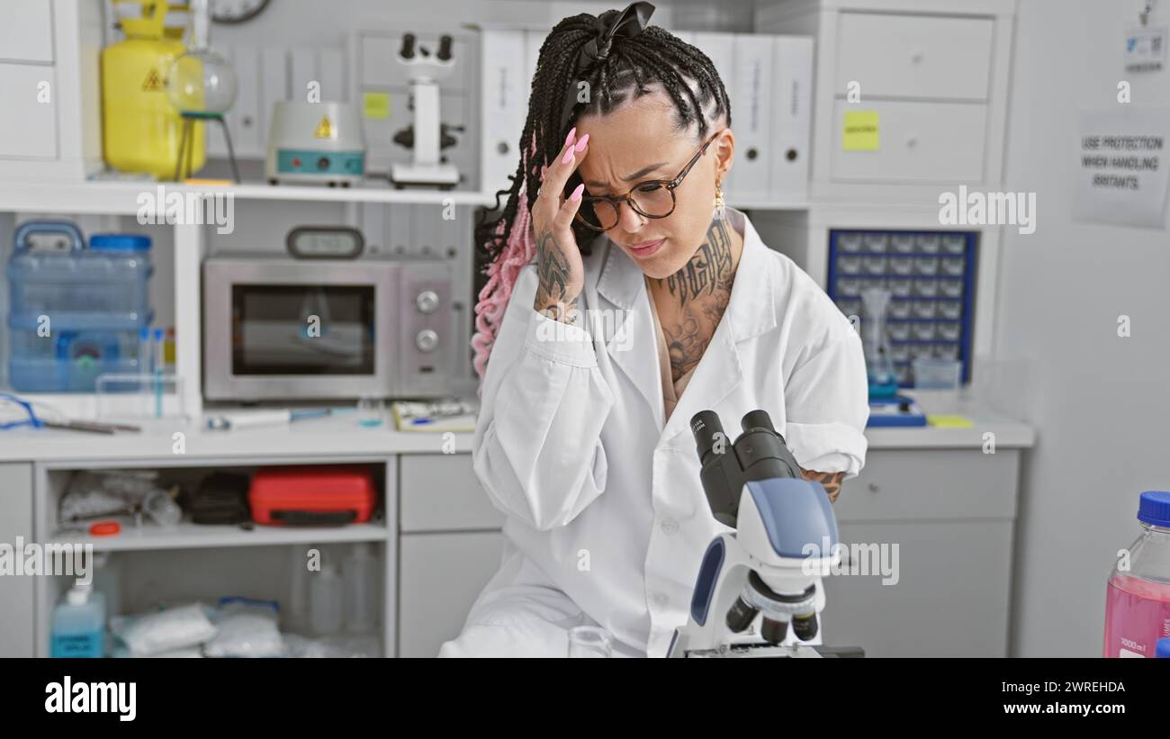 Stressed young hispanic woman scientist struggles with microscope ...