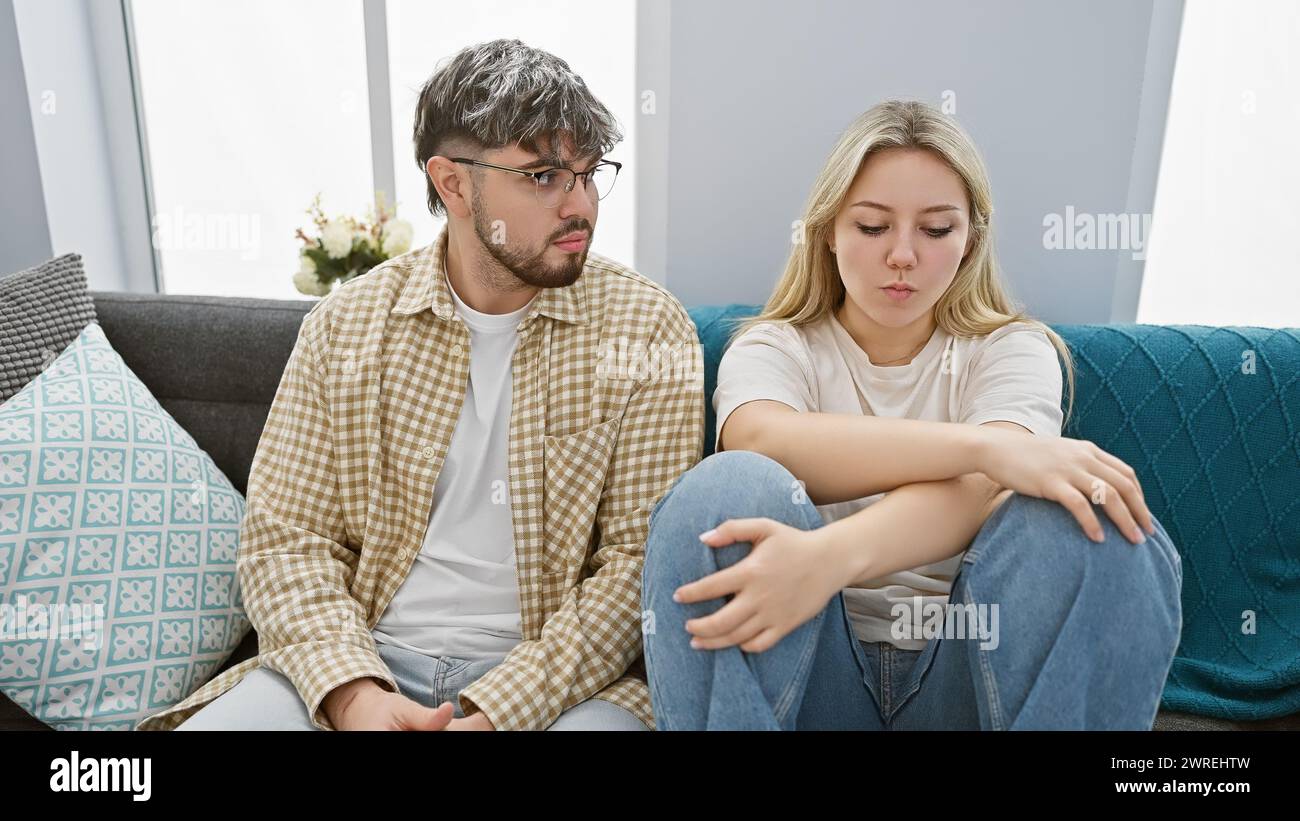 A man and woman sit apart on a couch, depicting tension or disagreement ...
