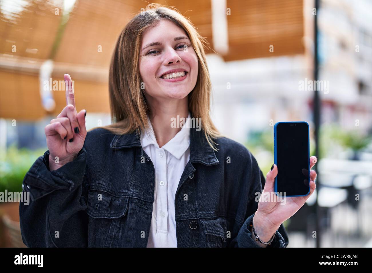 Excited, young blonde woman, holding smartphone, beams with brilliant ...