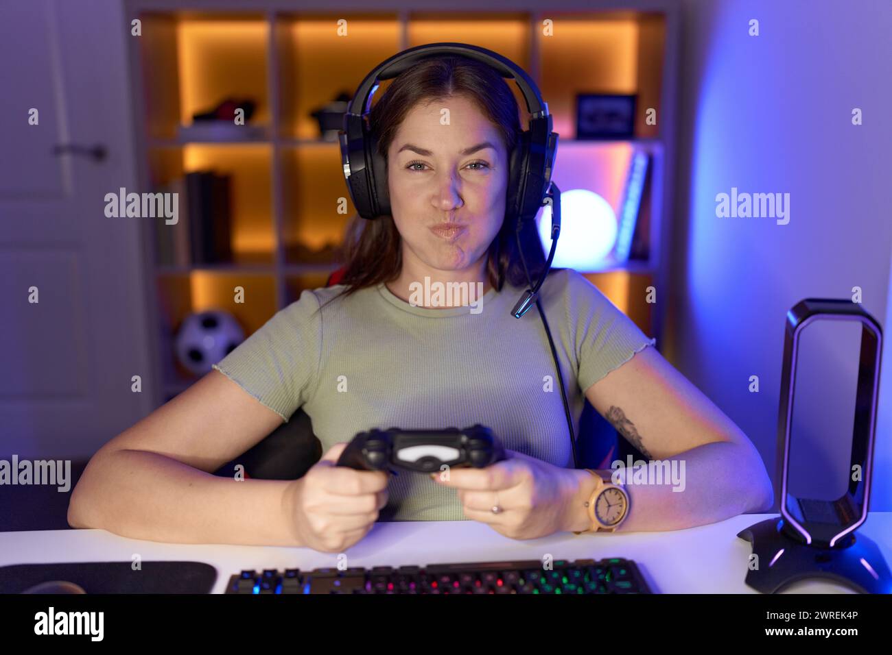 Beautiful brunette woman playing video games wearing headphones puffing ...