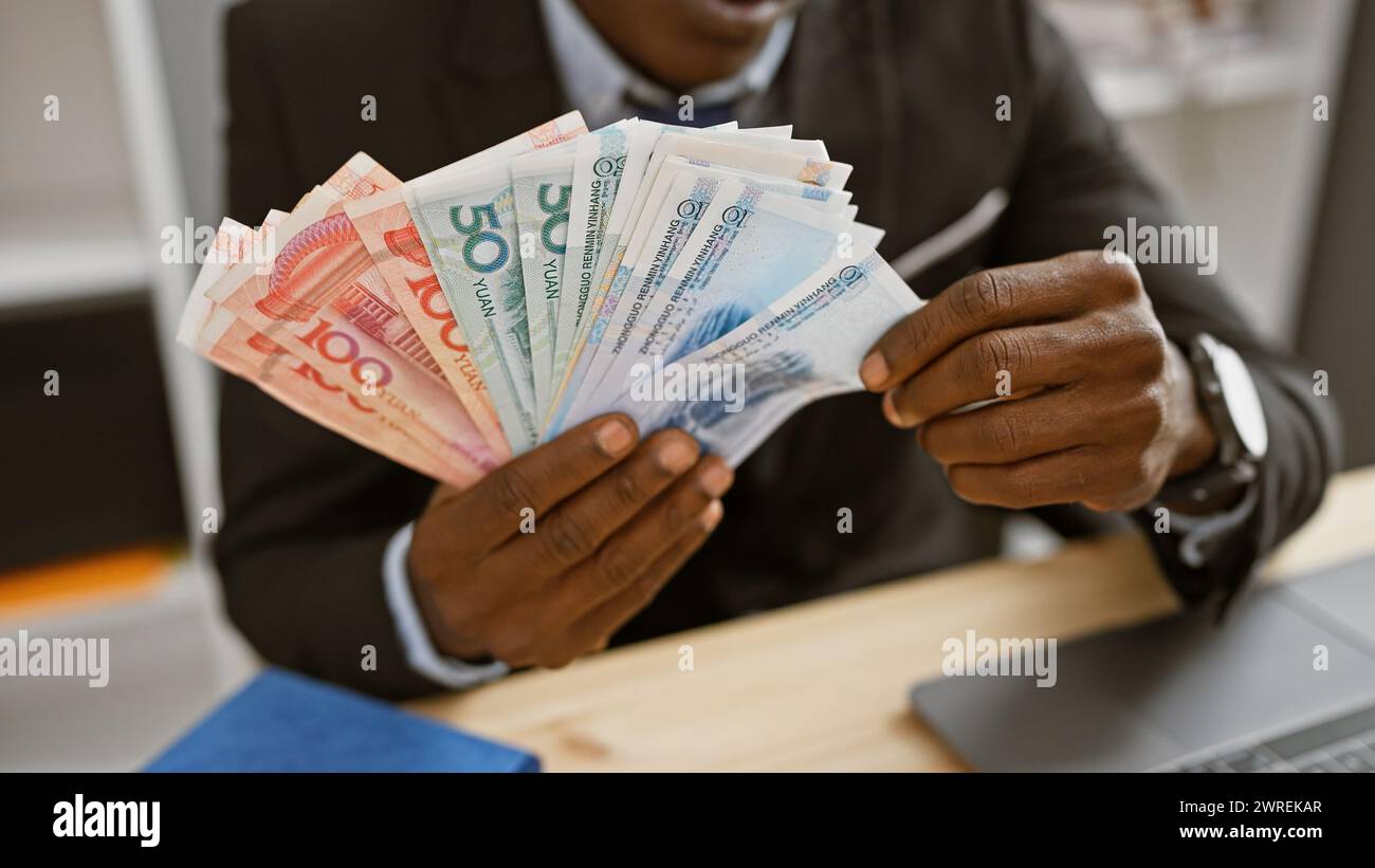 African man counting chinese yuan in a modern office setting ...