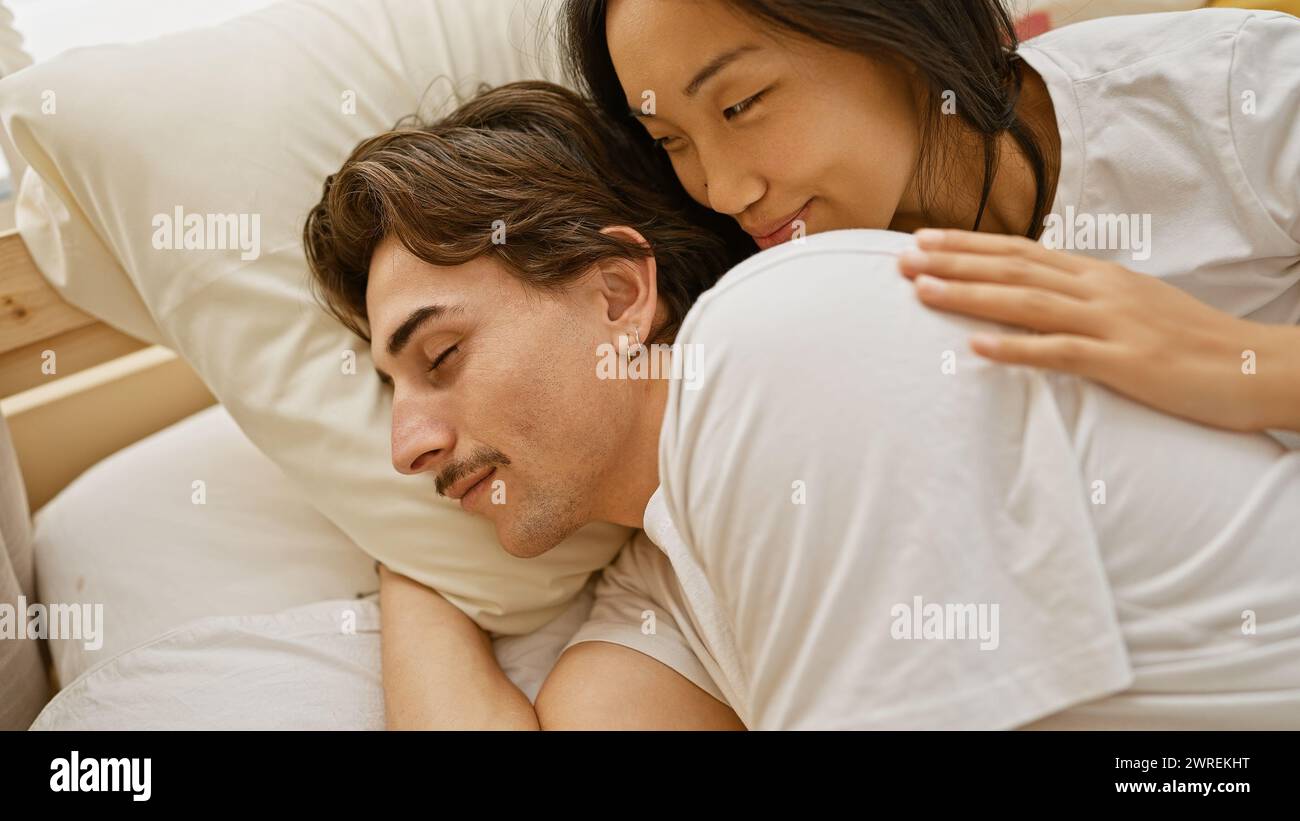 A loving interracial couple cuddling in a cozy bedroom setting ...