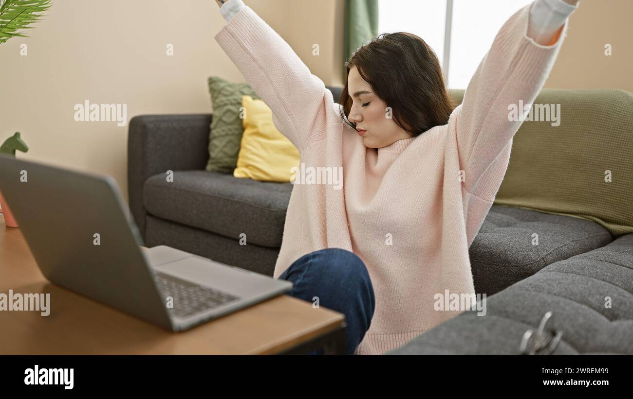 A relaxed young woman stretches while taking a break from her laptop in ...