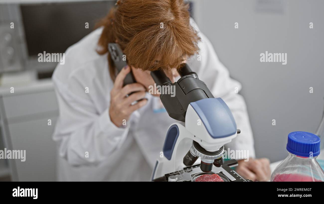 A mature woman multitasks in a laboratory, observing a specimen through ...