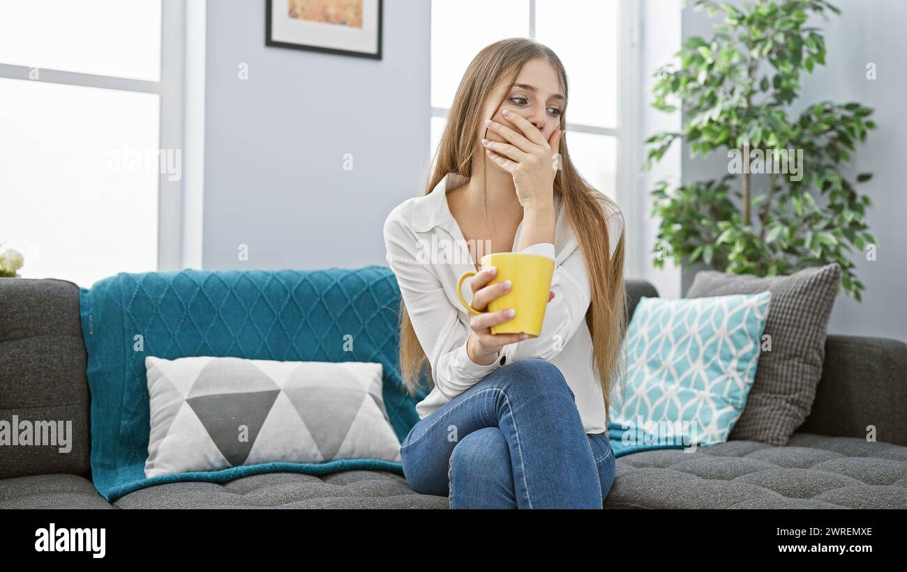 A surprised young caucasian woman in casual clothing sitting on a couch ...