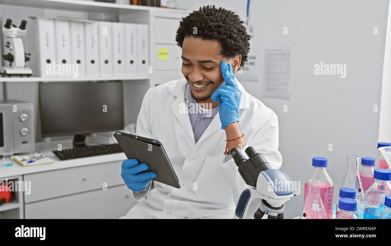 A smiling young man in lab coat using tablet in modern laboratory ...