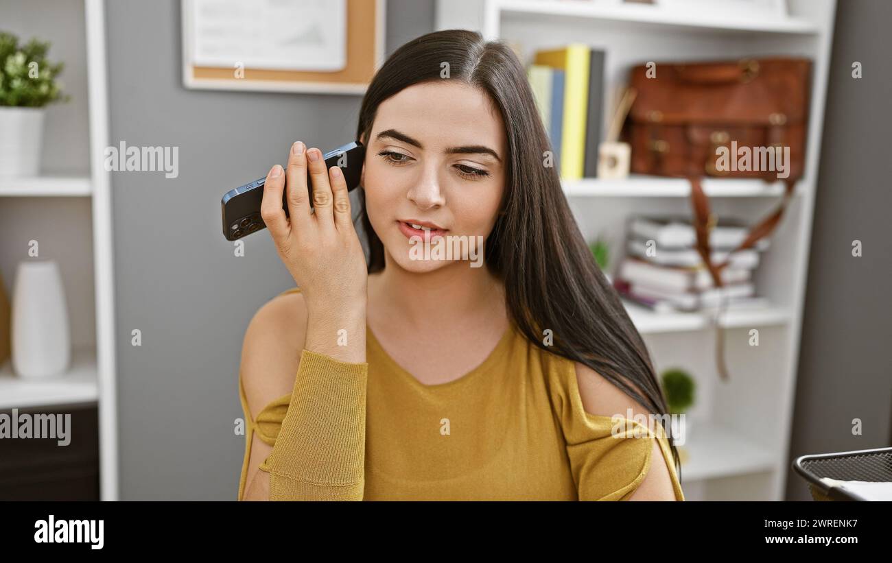 A young hispanic woman listens to a voice message in an office setting ...
