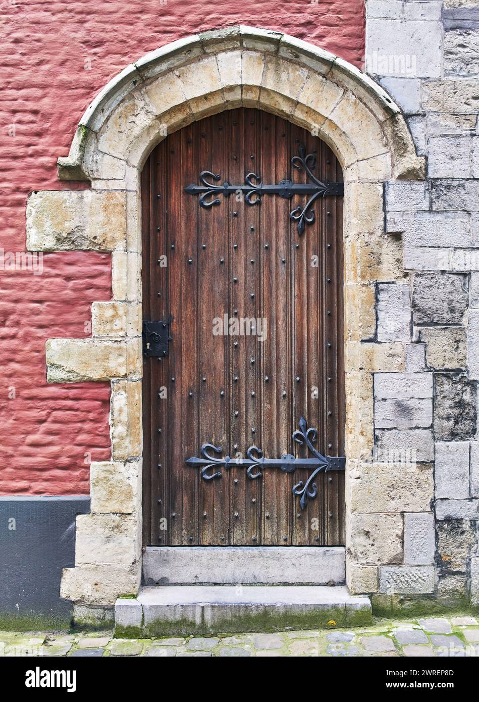 Ancient wooden door with iron hinges on a textured red wall, typical in ...