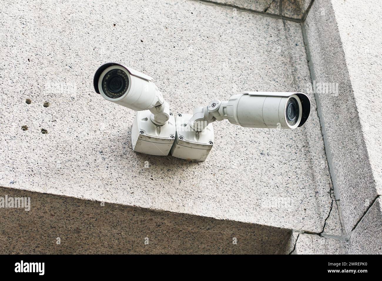 Two white surveillance cameras attached to a grey concrete building ...