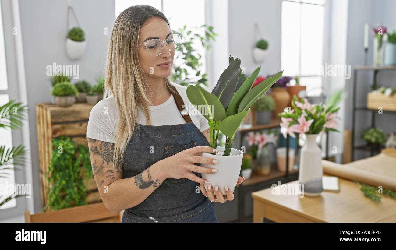 A caucasian woman florist in an apron holding a plant admires her work ...